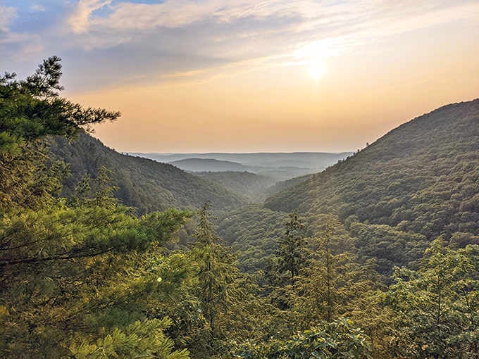 Misty mountains roll into the distance under a golden sunset, painting layers of ridges in soft purple and blue hues.