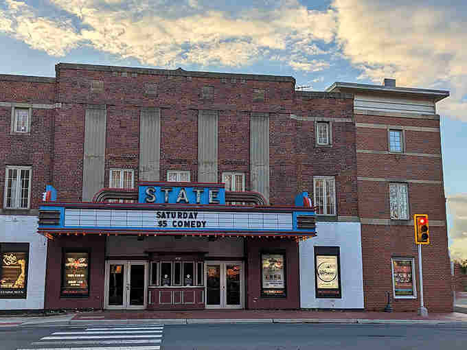 That vintage State Theatre marquee glows with promise, offering live comedy where Hollywood once flickered on silver screens.