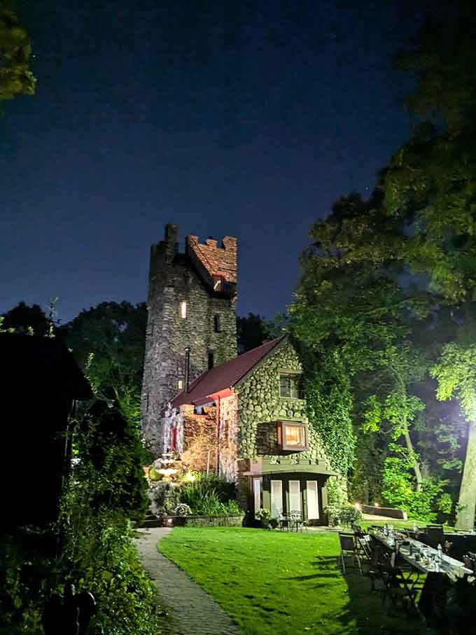 Evening lights illuminate the castle's rough stone walls, creating an enchanted glow against the darkening summer sky.