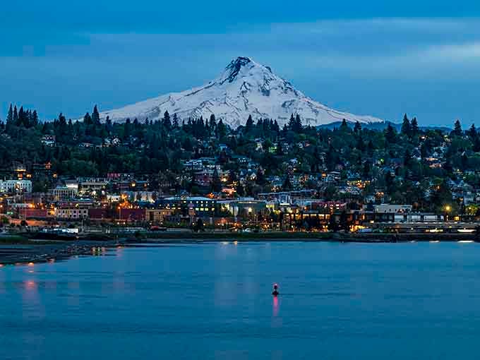 Twinkling town lights reflect on the Columbia River as Mount Hood stands sentinel over this magical evening scene.