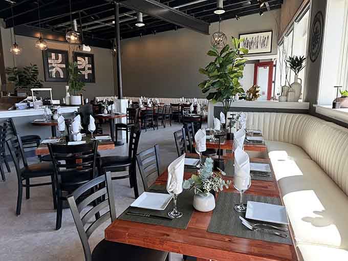 The modern interior blends industrial chic with comfort, where crisp linens and greenery set the stage for culinary excellence.