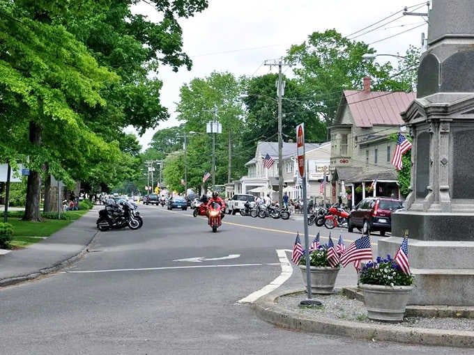 Motorcycles roll past patriotic displays on a street where small-town pride runs deep and genuine.