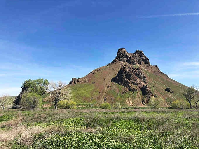 Spring brings fresh green grass to surround the ancient butte, softening the dramatic contrast between earth and that jagged stone tower.