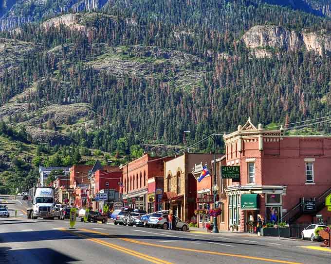 Historic storefronts march down the avenue where mountains tower overhead like protective stone sentinels watching forever.