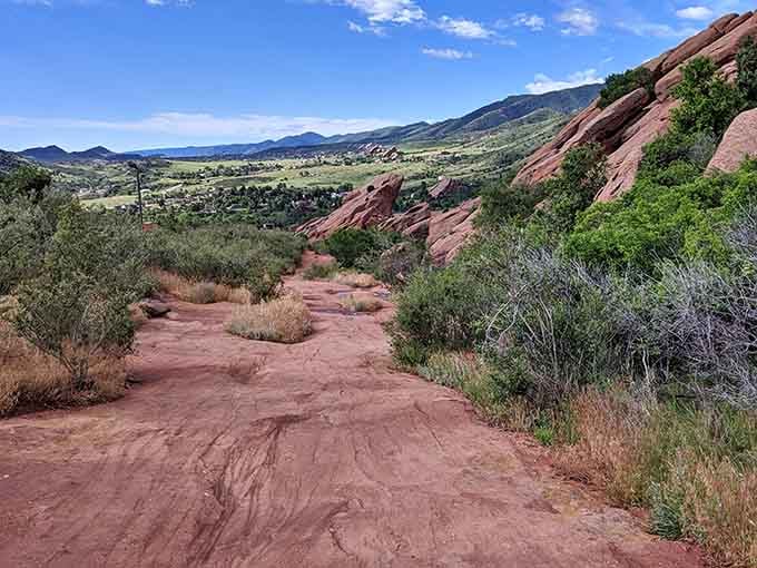 The dusty trail descends through scrubland, offering sweeping valley views that stretch clear to the distant horizon.