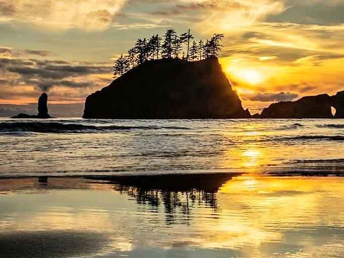 Sunset ignites the sky behind coastal rocks, turning the wet sand into liquid gold at your feet.