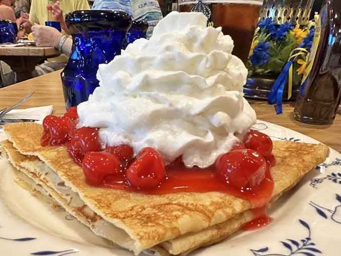 Swedish pancakes topped with cherries and whipped cream tower like a delicious monument to breakfast excellence.