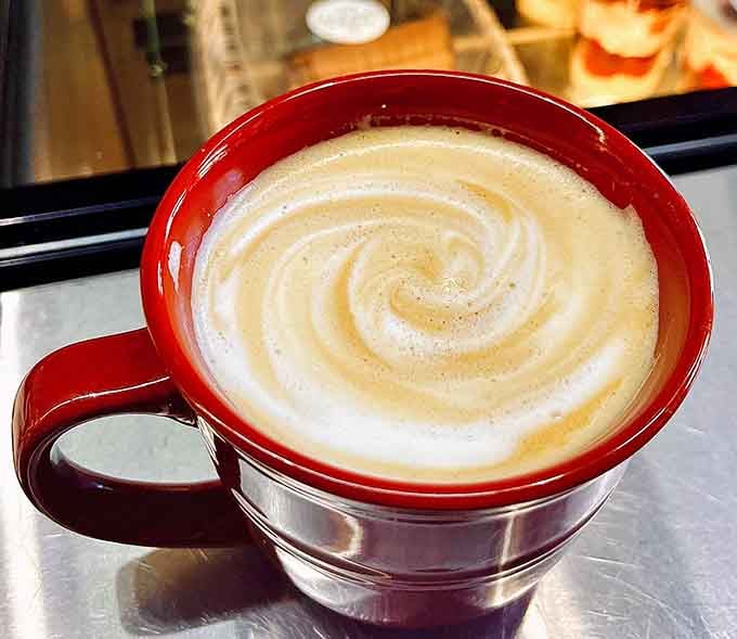 Swirled foam art in a crimson mug means someone here takes their coffee as seriously as their pastries.
