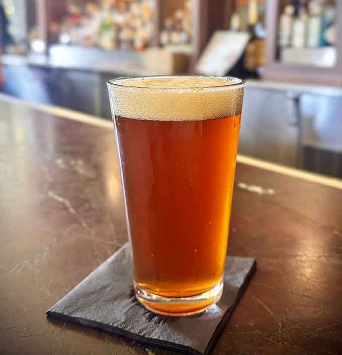 A perfectly poured amber beer catching the light at the bar, which is basically art you can drink and nobody judges you for it.