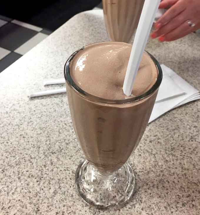 That chocolate milkshake stands tall in its classic glass, thick enough to require genuine effort and absolutely worth every sip.