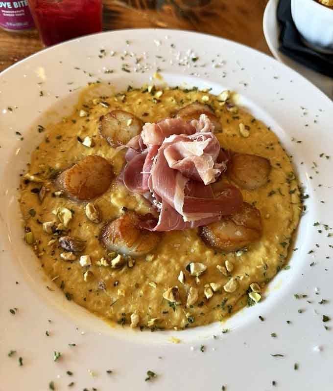Scallops swimming in what appears to be a golden dream sauce with prosciutto on top – fancy never tasted so good.