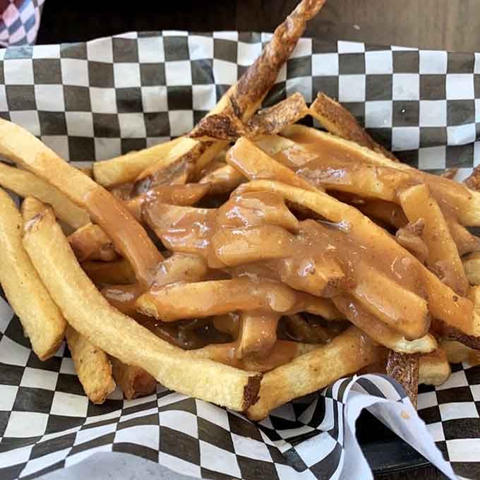 French fries swimming in gravy like they're at the world's most delicious pool party on checkered paper.