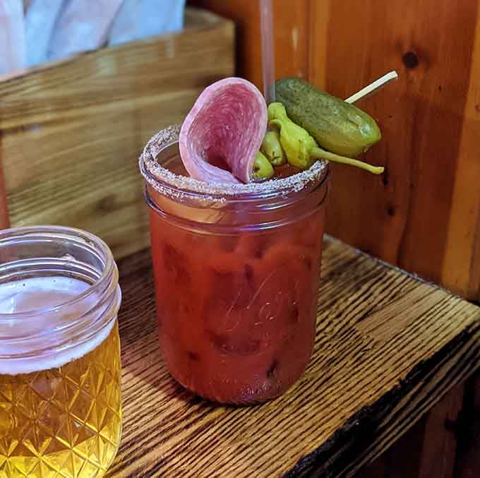 A Bloody Mary garnished like it's preparing for battle, complete with pickles, peppers, and enough salami to qualify as lunch.