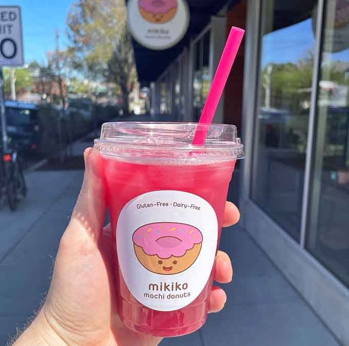 Bright pink hibiscus lemonade in a cup adorned with a smiling donut, because even your beverage should bring joy.