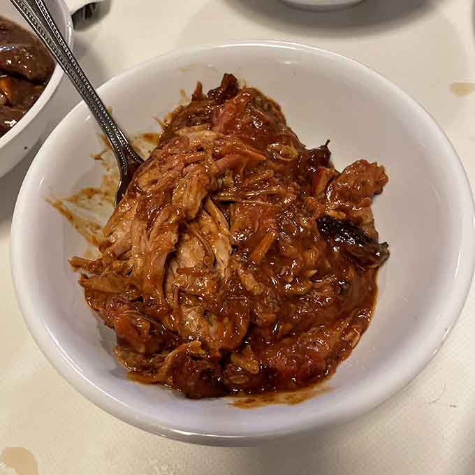Pulled pork swimming in sauce, the kind of tender, flavorful meat that requires strategic napkin placement before diving in.