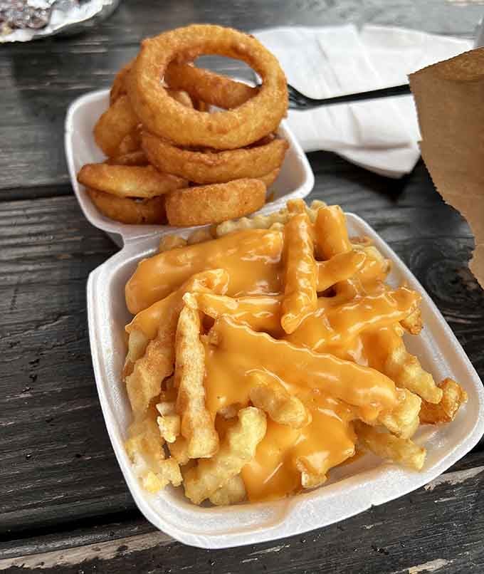 Golden fries drowning in cheese next to crispy onion rings, because sometimes more really is more.