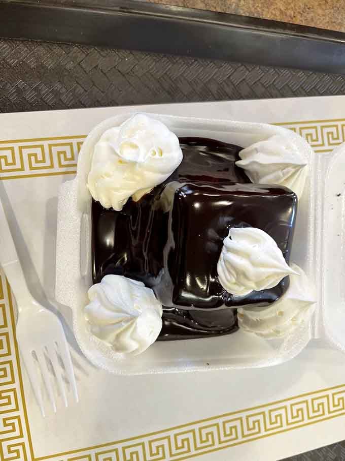 Dark chocolate fudge cascading over cake with whipped cream rosettes is basically happiness you can eat with a fork.