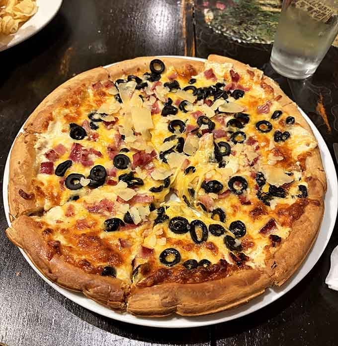 Pizza loaded with olives, bacon, and cheese that stretches like it's trying to escape your plate for freedom.