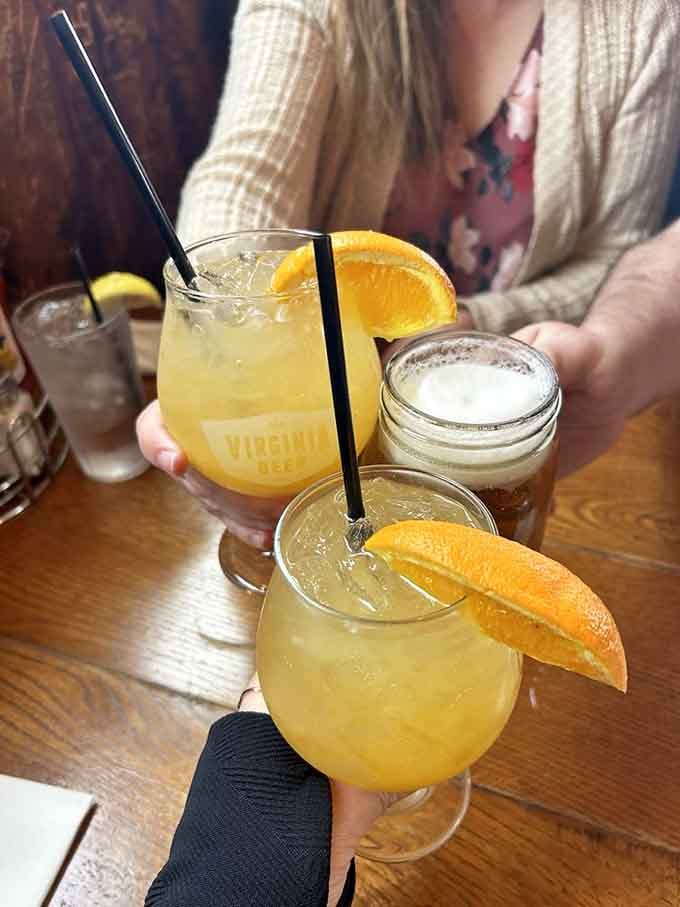 Orange-garnished cocktails catch the light while beer waits patiently, because good times require proper liquid accompaniment.