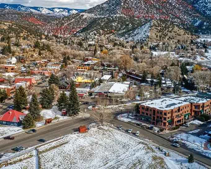 Winter dusts the rooftops while colorful buildings pop against snow-covered peaks in this cozy valley town.
