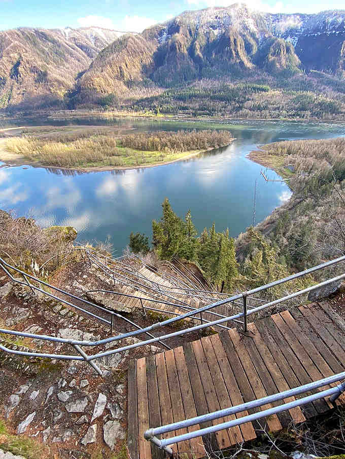 Wooden stairs descend toward mirror-like waters that reflect mountains so clearly you'll question which way is up.