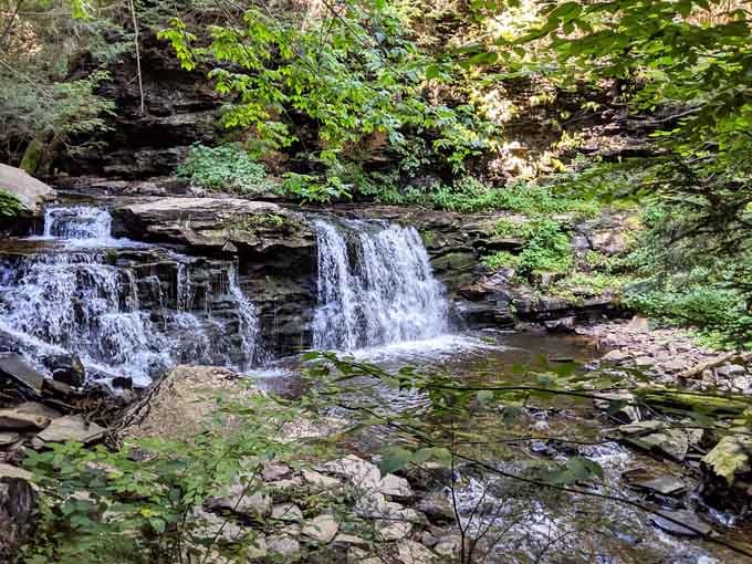 Water cascades over layered rock shelves in this forest glen where moss-covered stones frame nature's perpetual motion in perfect tranquility.
