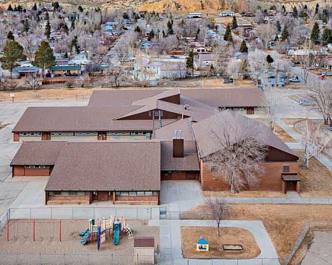 Mid-century educational architecture spreads across the landscape like a small village, its connected buildings and empty playground frozen in winter's quiet pause.