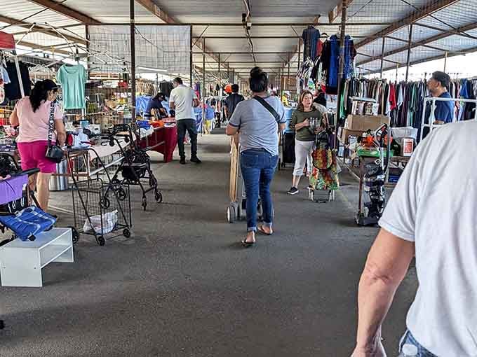 Shoppers meander past tables overflowing with clothing and toys while the metal roof overhead keeps everyone comfortable regardless of weather.