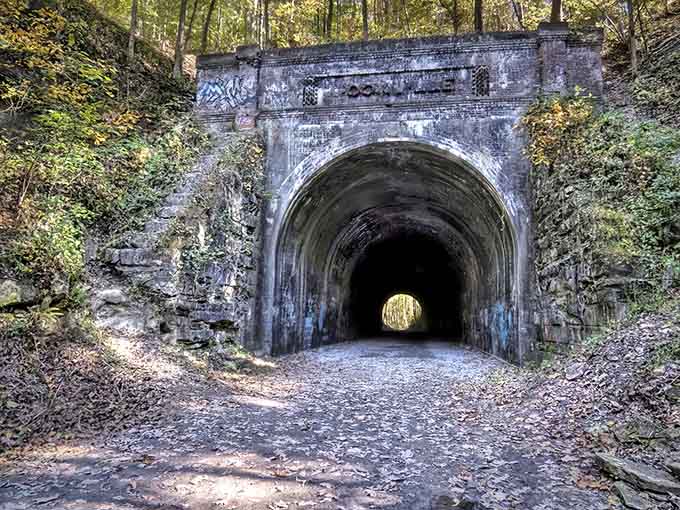 The weathered brick entrance stands guard over this abandoned railroad tunnel, now covered in colorful graffiti and local legends.