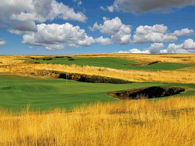 Wind-swept grasses frame emerald fairways where the landscape stretches endlessly under dramatic clouded skies above.