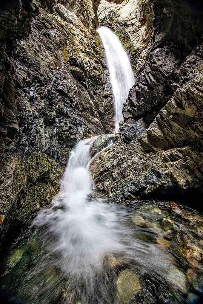 The waterfall plunges dramatically between dark stone walls, creating misty magic in this hidden slot canyon sanctuary.