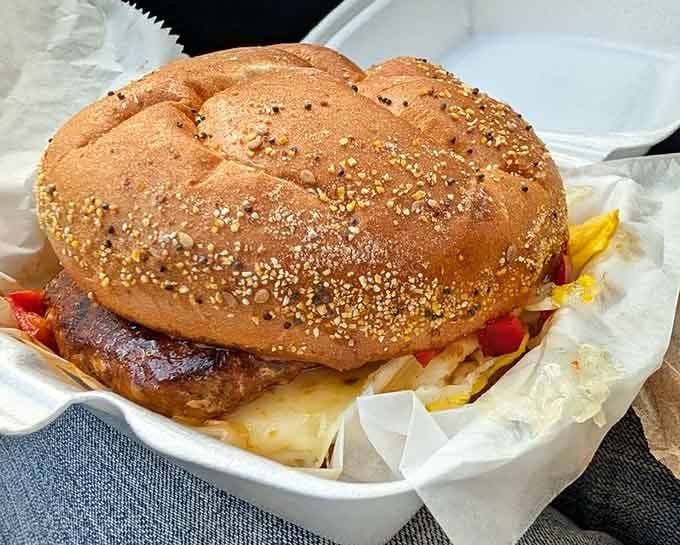 A sesame-topped bun barely containing its burger, cheese, and peppers like a delicious structural engineering challenge.