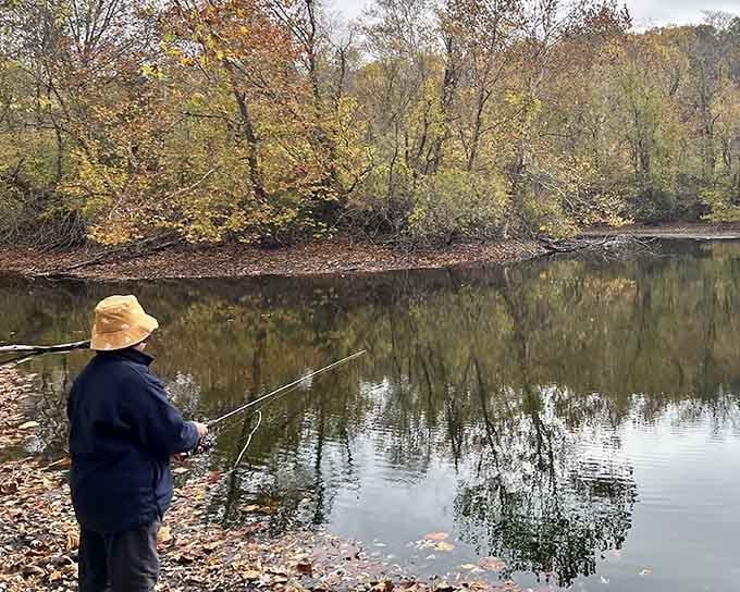 This angler has found the sweet spot where patience meets possibility, surrounded by fall's golden reflection on still water.