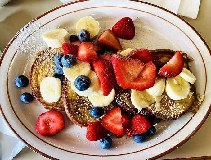 French toast buried under enough fresh fruit to qualify as both indulgence and vitamin delivery system simultaneously.