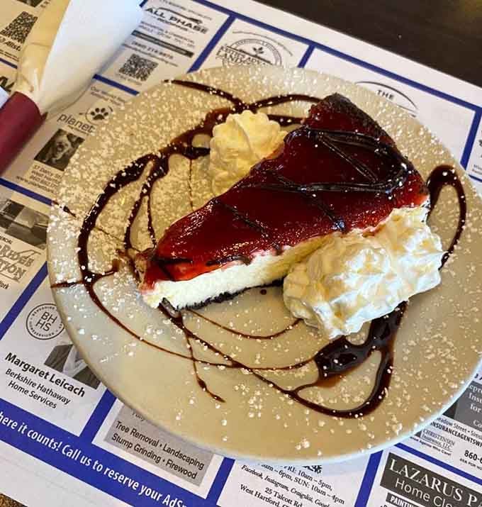 Cheesecake drizzled with ruby-red topping and chocolate sauce, proving dessert doesn't care what meal you just finished eating.