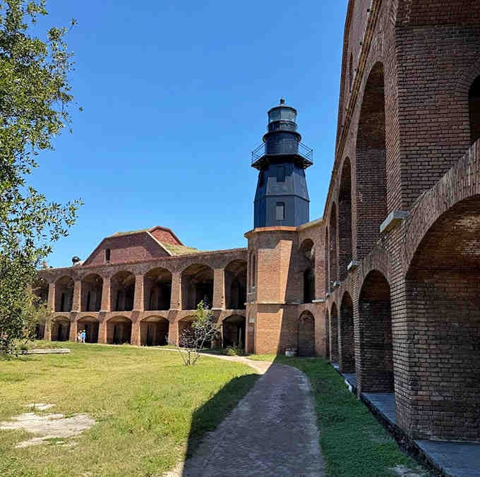 The lighthouse stands guard over the courtyard, a black exclamation point against endless blue sky and weathered red brick.