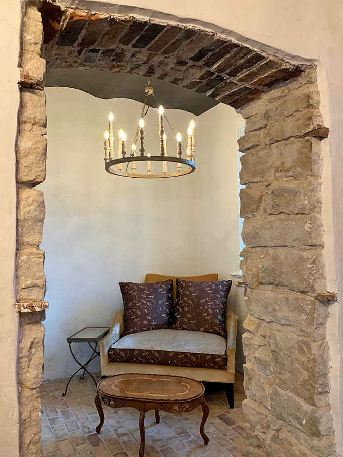 Thick stone archways frame intimate spaces where chandeliers cast their warm glow on plush seating below.