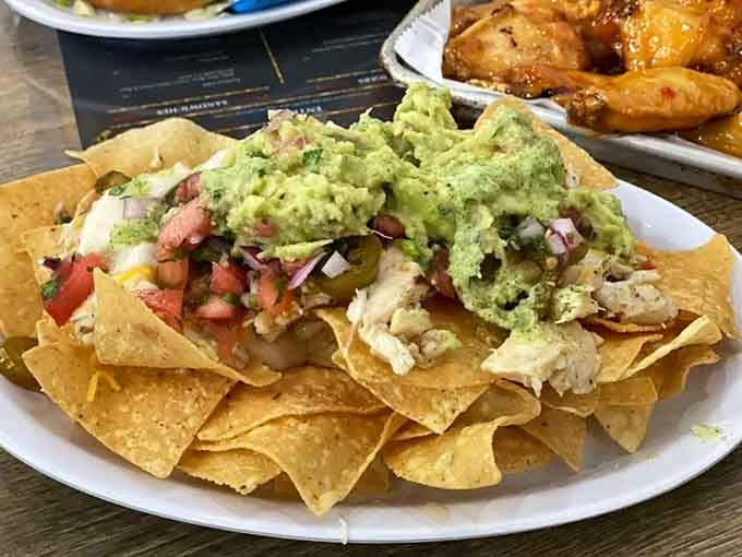 Nachos buried under guacamole and toppings create a mountain of melted cheese happiness that demands immediate attention and napkins.