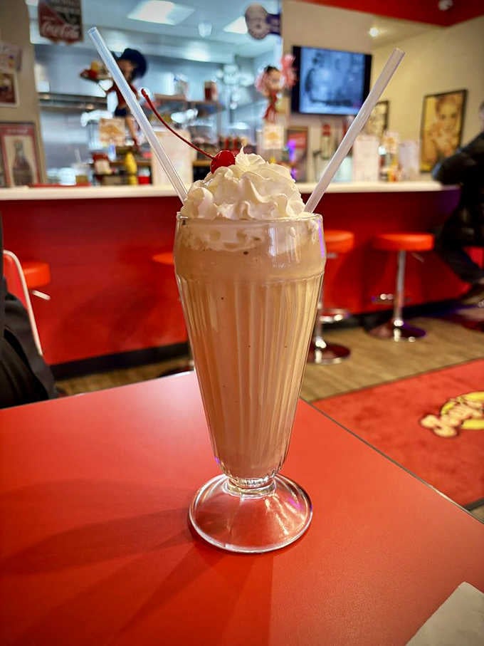 A chocolate malt topped with whipped cream and a cherry, served in a glass that demands two straws.