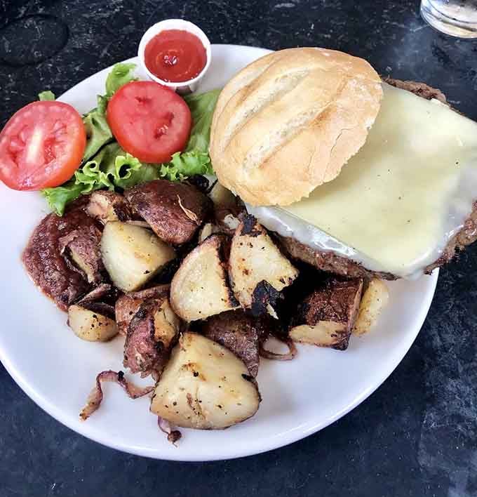 Thick slices of tomato, crisp lettuce, and golden potatoes accompany a cheese-blanketed burger that means serious business at lunchtime.