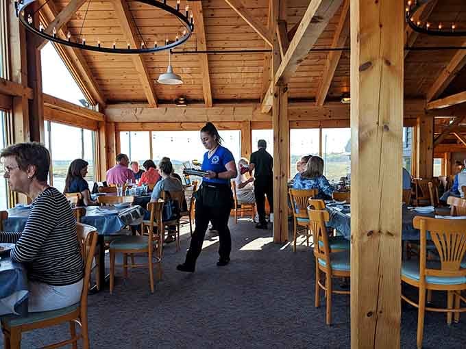 Diners enjoying their meals with those massive windows showcasing why waterfront dining beats landlocked restaurants every single time.