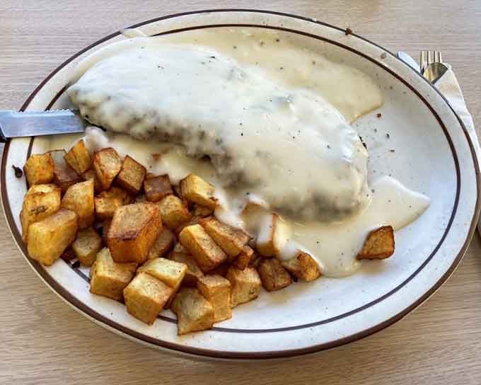 Country fried steak smothered in peppery gravy alongside golden potatoes, breakfast done the old-fashioned way right.