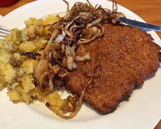 Golden schnitzel crowned with caramelized onions and herbed potatoes, making you forget every mediocre pork chop you've ever endured.