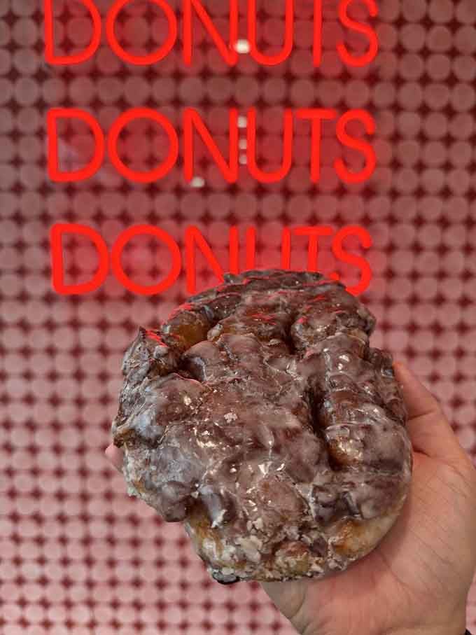 An apple fritter held in hand, covered in glaze, representing everything right about breakfast pastries.