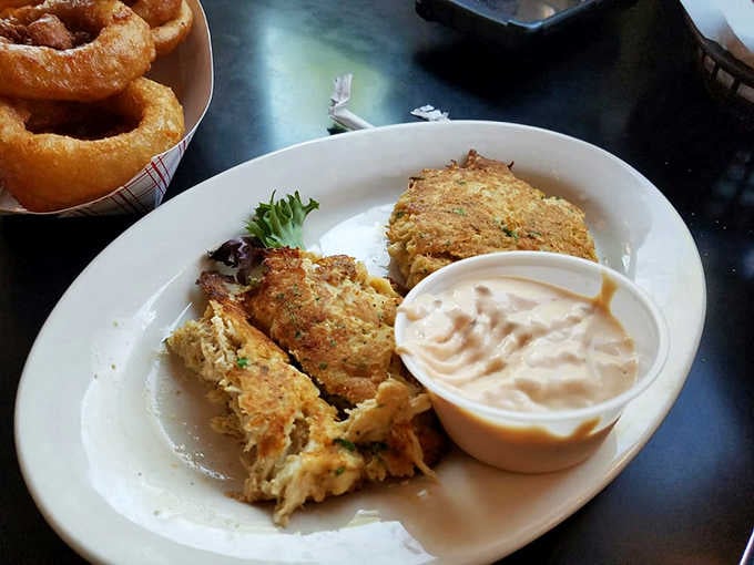 Golden crab cakes served with a side of onion rings, because apparently someone understood the assignment perfectly.
