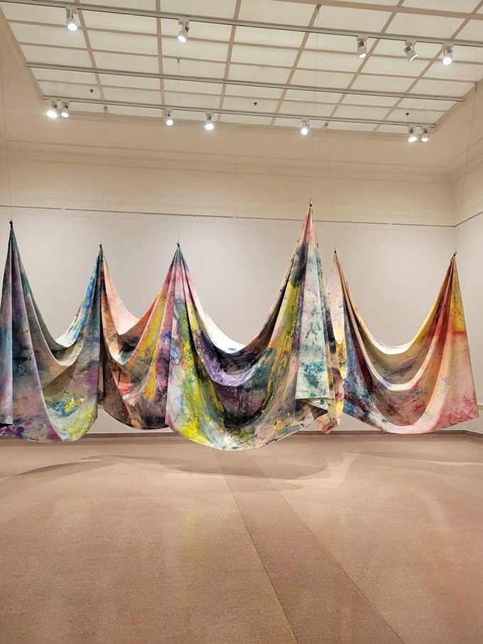 Massive painted fabric drapes cascade across the floor like frozen waterfalls of color and creative energy unleashed.
