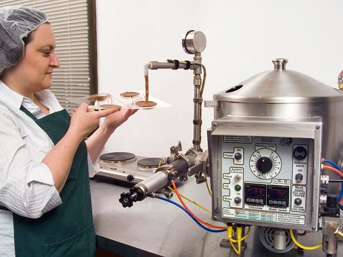 Real chocolate craftsmanship happens here, where skilled hands guide molten chocolate through gleaming tempering equipment with practiced precision.