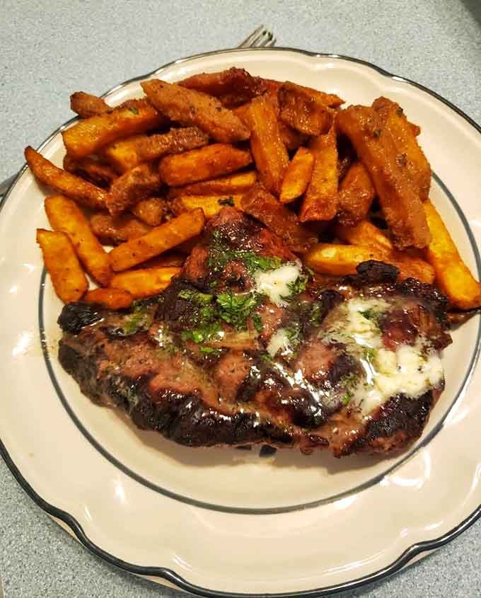 A beautifully charred steak topped with melted cheese and surrounded by crispy fries delivers pure comfort food satisfaction.
