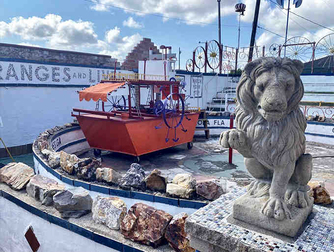 A concrete lion guards a miniature ship because in folk art, logic takes a permanent vacation.