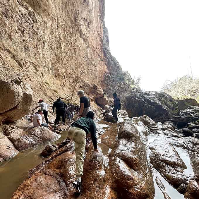 Hikers navigate wet rocks beneath soaring canyon walls, proving the best views require a little careful footwork.